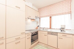 Cozinha com armários em tons claros, micro-ondas, forno, lava-louças e janela com valance listrado.