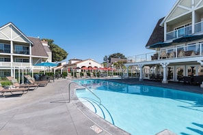 Piscina com espreguiçadeiras e guarda-sóis, cercada por edifícios com varandas e áreas de estar ao ar livre.