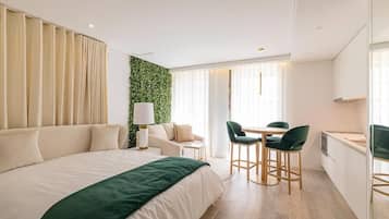 Quarto de hotel moderno com uma cama grande, um espaço pequeno para refeições e uma cozinha compacta.