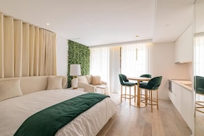 Quarto de hotel moderno com uma cama grande, um espaço pequeno para refeições e uma cozinha compacta.