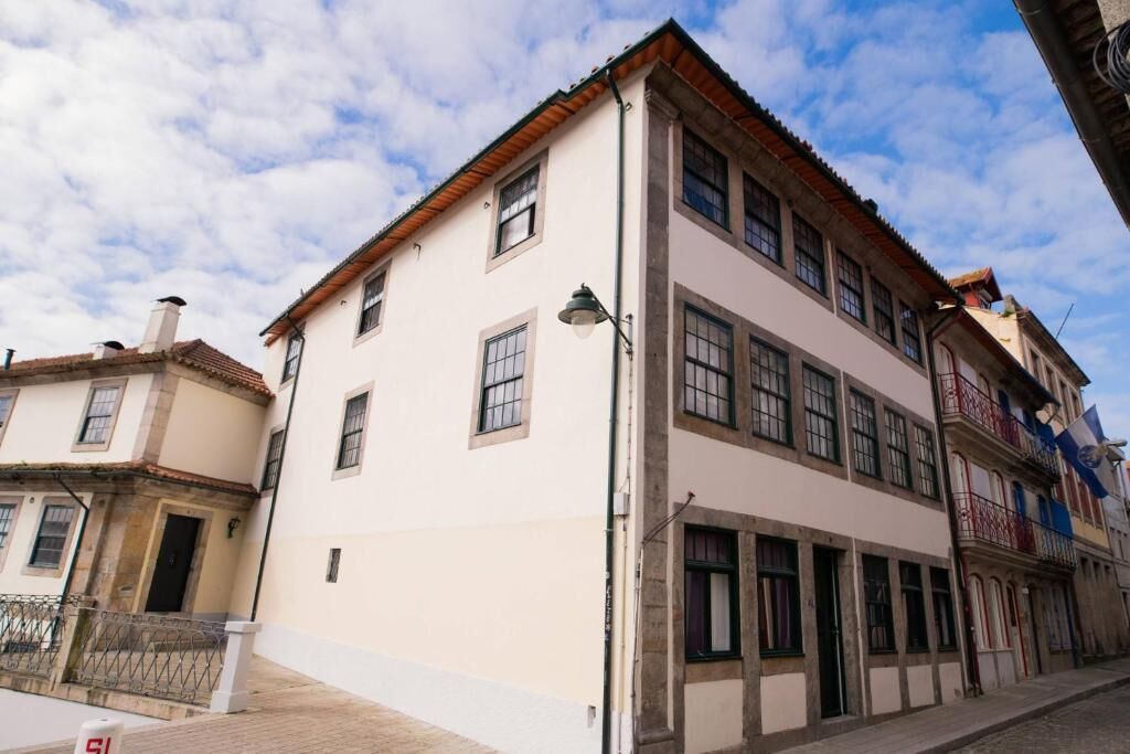 Um edifício de dois andares com fachada branca, várias janelas e telhado em telhas.