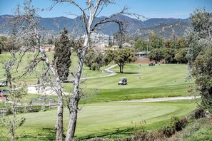 Um campo de golfe com vista ampla da paisagem circundante, incluindo montanhas e edifícios ao longe.