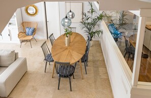 Uma área de refeições com uma mesa de madeira redonda, cadeiras e plantas em vasos.