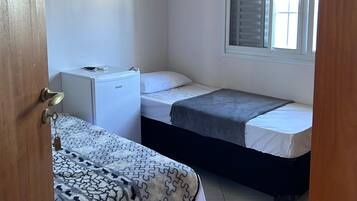 Quarto com duas camas, um ar condicionado branco, uma janela com persianas e uma porta com puxador de latão.