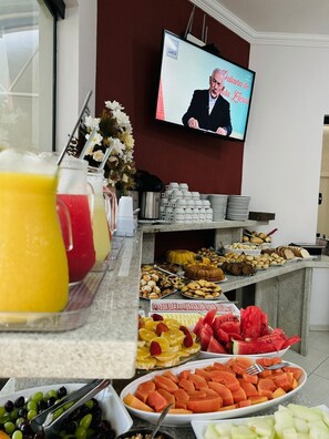 Buffet com diversos alimentos e uma televisão ao fundo.