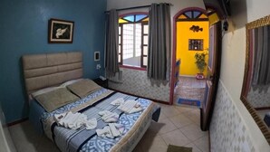 Quarto com cama, ventilador de teto, televisão na parede e janela com cortinas.