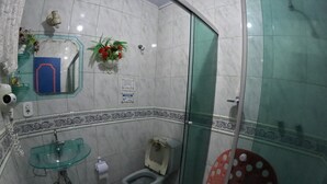 Casa de banho com chuveiro em cabine de vidro, sanita, lavatório e espelho.