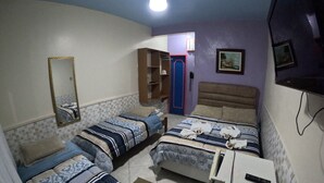 Quarto com duas camas, um guarda-roupa, ventoinha no teto, porta e televisão presa na parede.