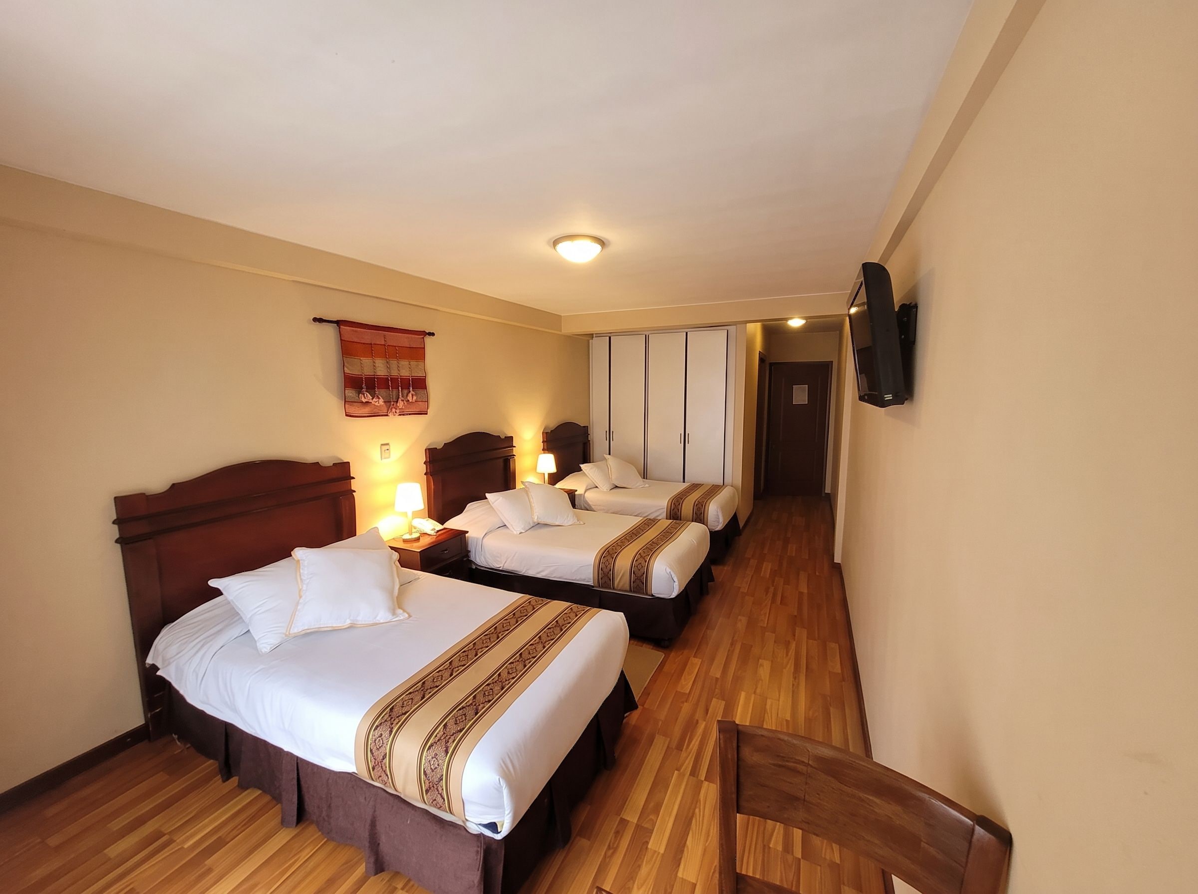 Quarto de hotel com duas camas, piso de madeira, televisão na parede e toalha listrada em vermelho e branco.