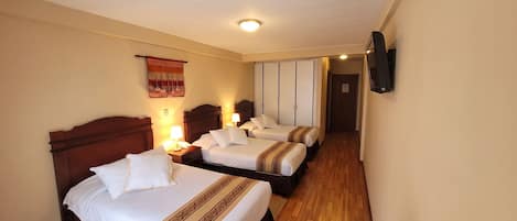 Quarto de hotel com duas camas, piso de madeira, televisão na parede e toalha listrada em vermelho e branco.