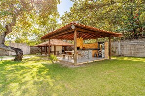 Uma área de estar coberta ao ar livre, com parede de tijolos e uma árvore ao fundo.