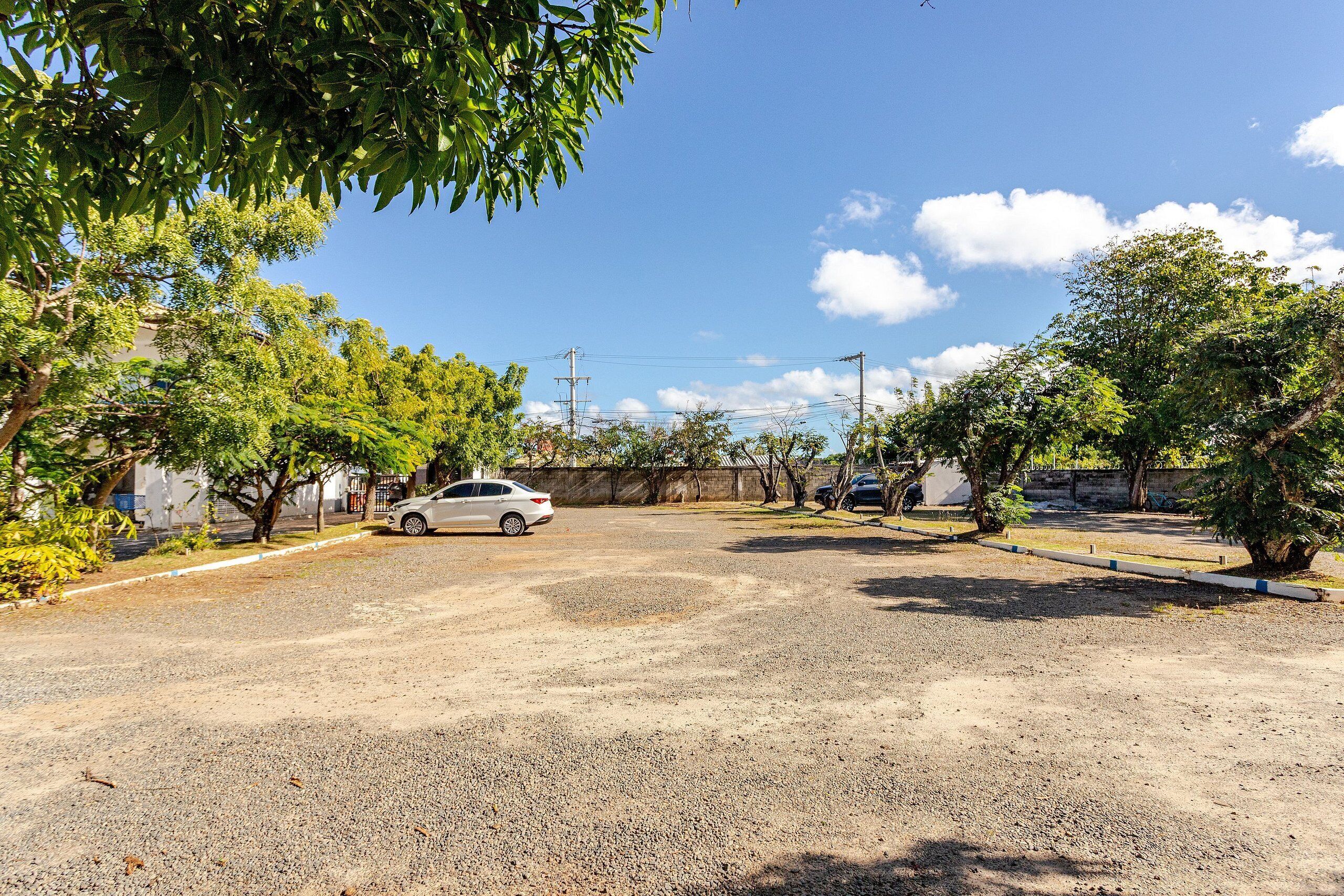 Uma área de estacionamento com um carro branco, cercada por árvores e um céu claro.