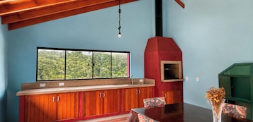 Uma cozinha com armários de madeira, forno vermelho e janela com vista para o verde.