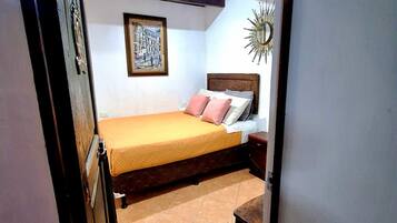 Quarto com cama, mesa de cabeceira, espelho fixado na parede e quadro emoldurado.