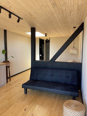 Quarto com sofá azul escuro, piso de madeira, escada e luminária pendente.