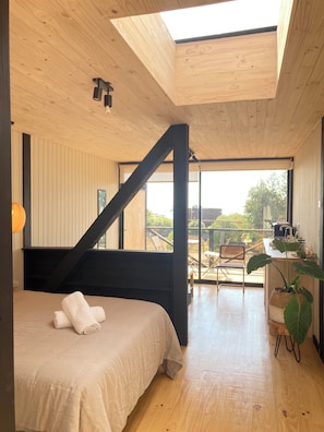 Quarto com cama, claraboia, escada e vista para o exterior.