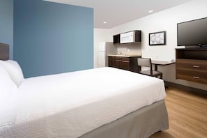Quarto de hotel com cama, escrivaninha, cadeira, televisão e micro-ondas.