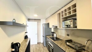 Cozinha compacta com geladeira embutida, micro-ondas e cafeteira no balcão.