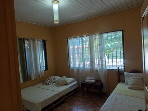 Quarto com duas camas, uma mesinha e uma janela com cortinas.