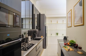 Uma cozinha moderna com forno embutido, pia de aço inoxidável e bancada com chaleira e taça de vinho.
