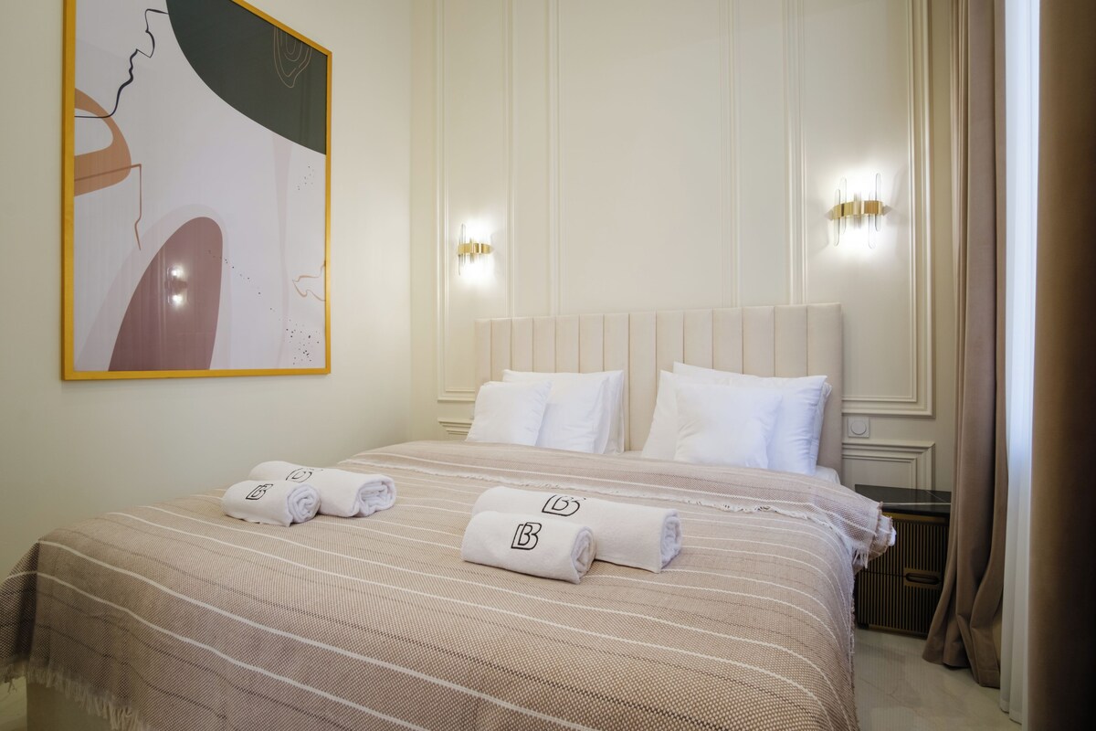 Quarto de hotel com uma cama grande, duas luminárias de cabeceira e um quadro na parede.