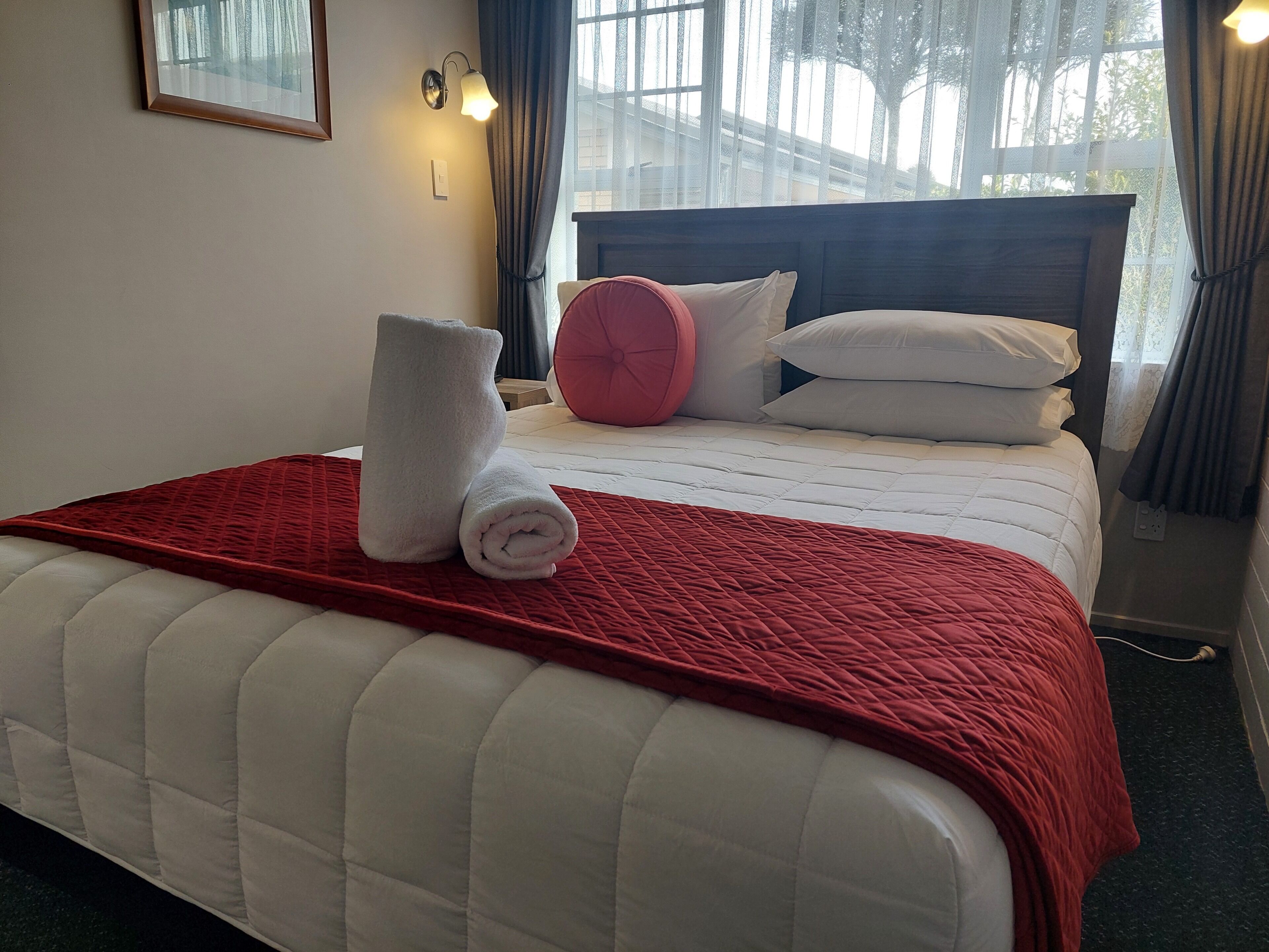 Quarto de hotel com uma cama, um cobertor vermelho e uma almofada branca.