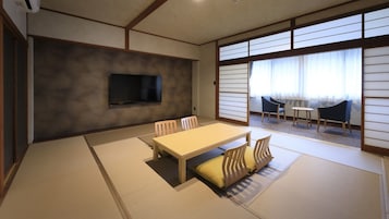 Um quarto em estilo japonês tradicional, com tatames, uma mesa baixa com cadeiras, uma televisão presa à parede e uma porta de tela deslizante shoji.