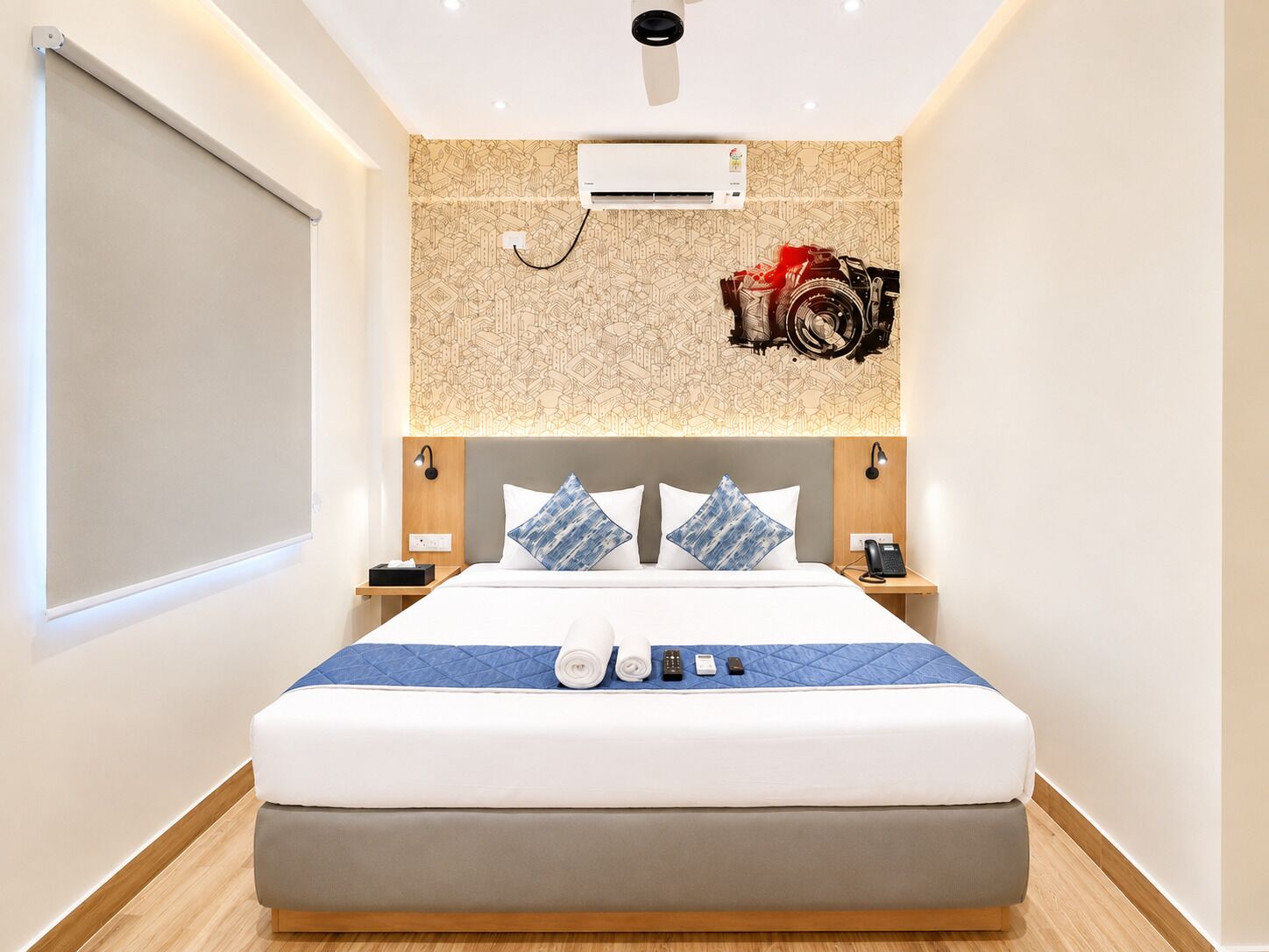 Quarto de hotel com cama, mesas de cabeceira, unidade de ar condicionado e câmera fixada na parede.