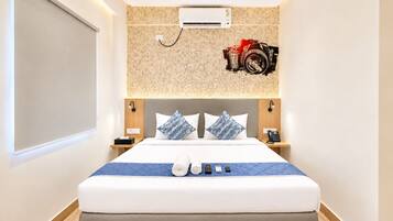 Quarto de hotel com cama, mesas de cabeceira, unidade de ar condicionado e câmera fixada na parede.