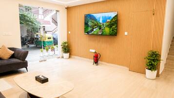 Uma sala de estar moderna com uma TV de tela plana numa parede de madeira, um sofá, uma mesa de centro e plantas em vasos.