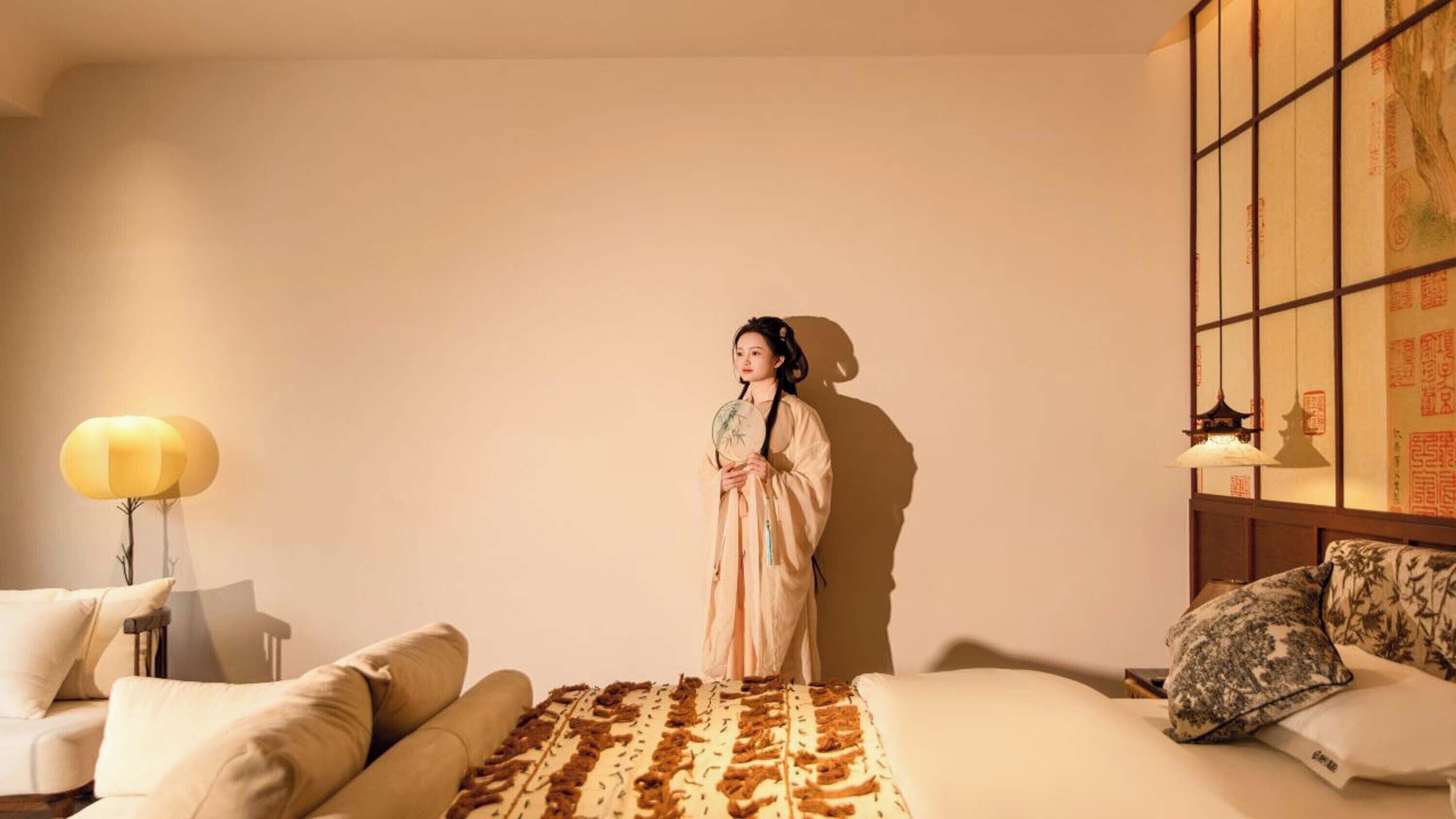 Quarto de hotel com cama, sofá, luminária e painel decorativo na parede.
