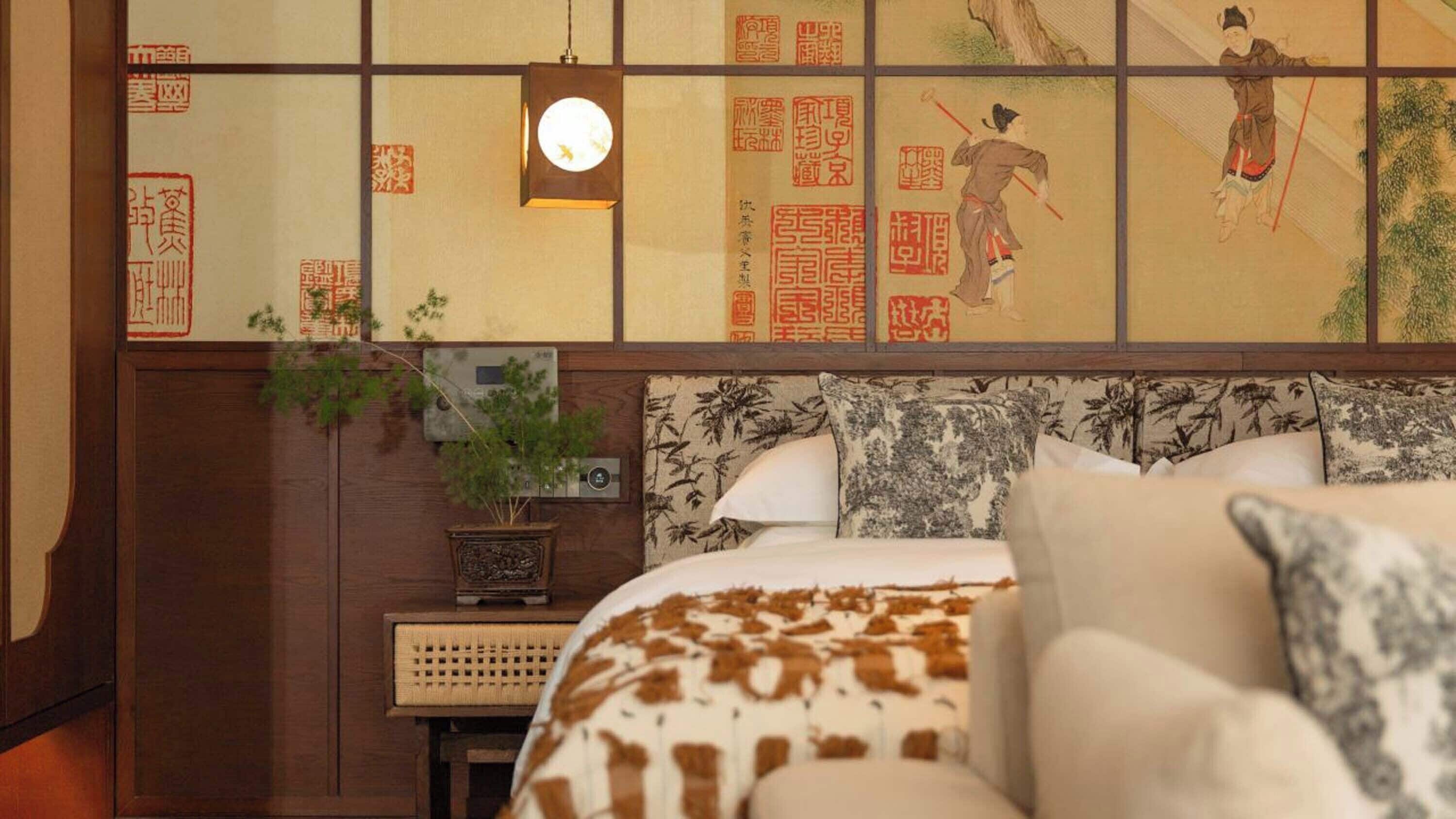 Um quarto tradicional japonês com tatames, um armário de madeira baixo, uma cama com cabeceira estampada e uma parede com caligrafia e pinturas.