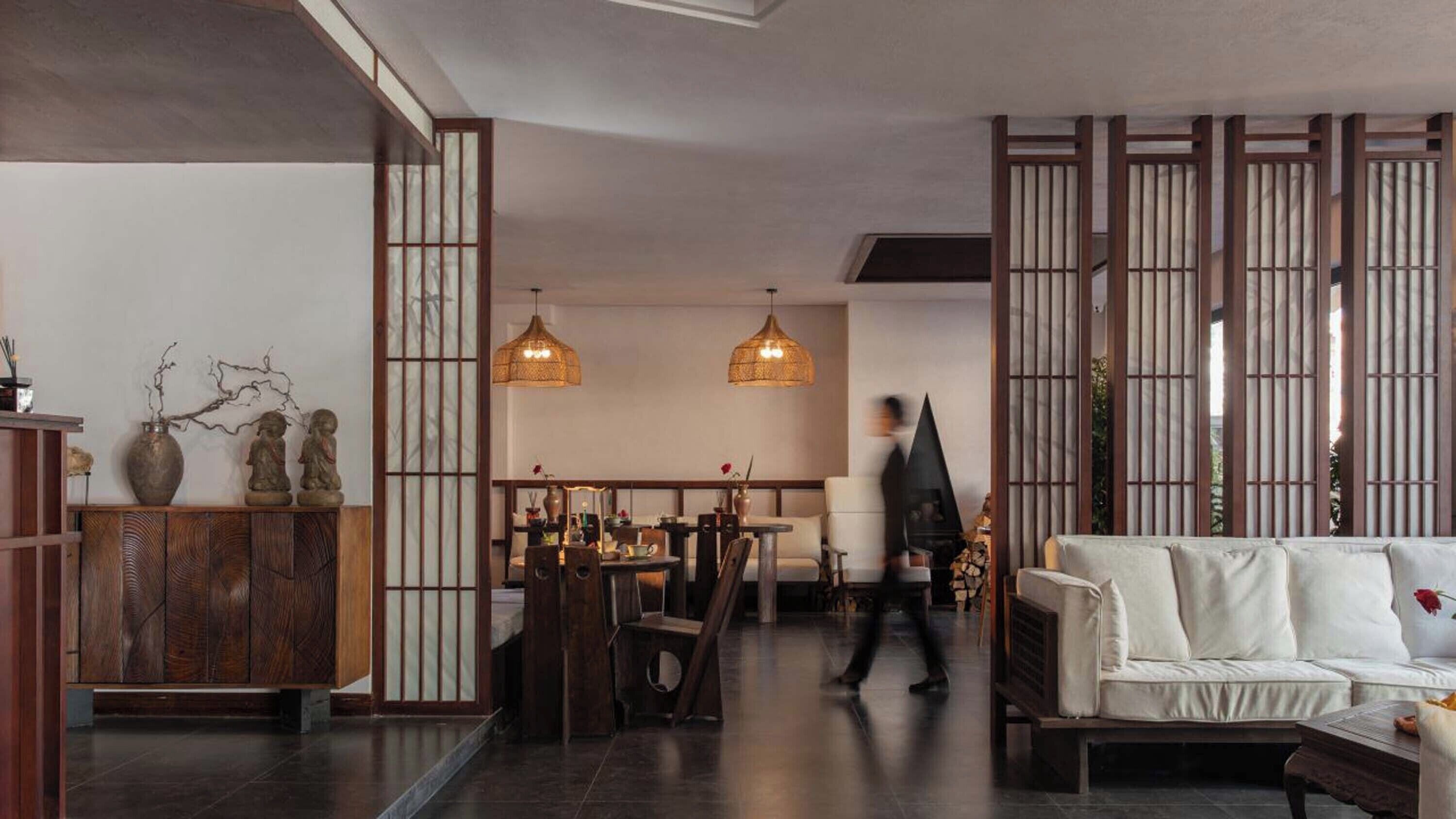 Um interior moderno com área de refeições, um sofá e uma pessoa caminhando.