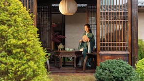 Um edifício em estilo tradicional chinês, com porta e grade de janela de madeira, uma mesa com utensílios de chá e um lanterna pendurada.