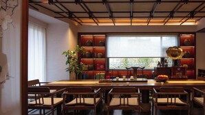 Uma sala de jantar com uma mesa comprida e cadeiras, um vaso de planta e uma janela com vista.