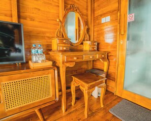 Um quarto de madeira com televisão, uma cômoda de madeira com gavetas, um espelho e um banquinho pequeno.