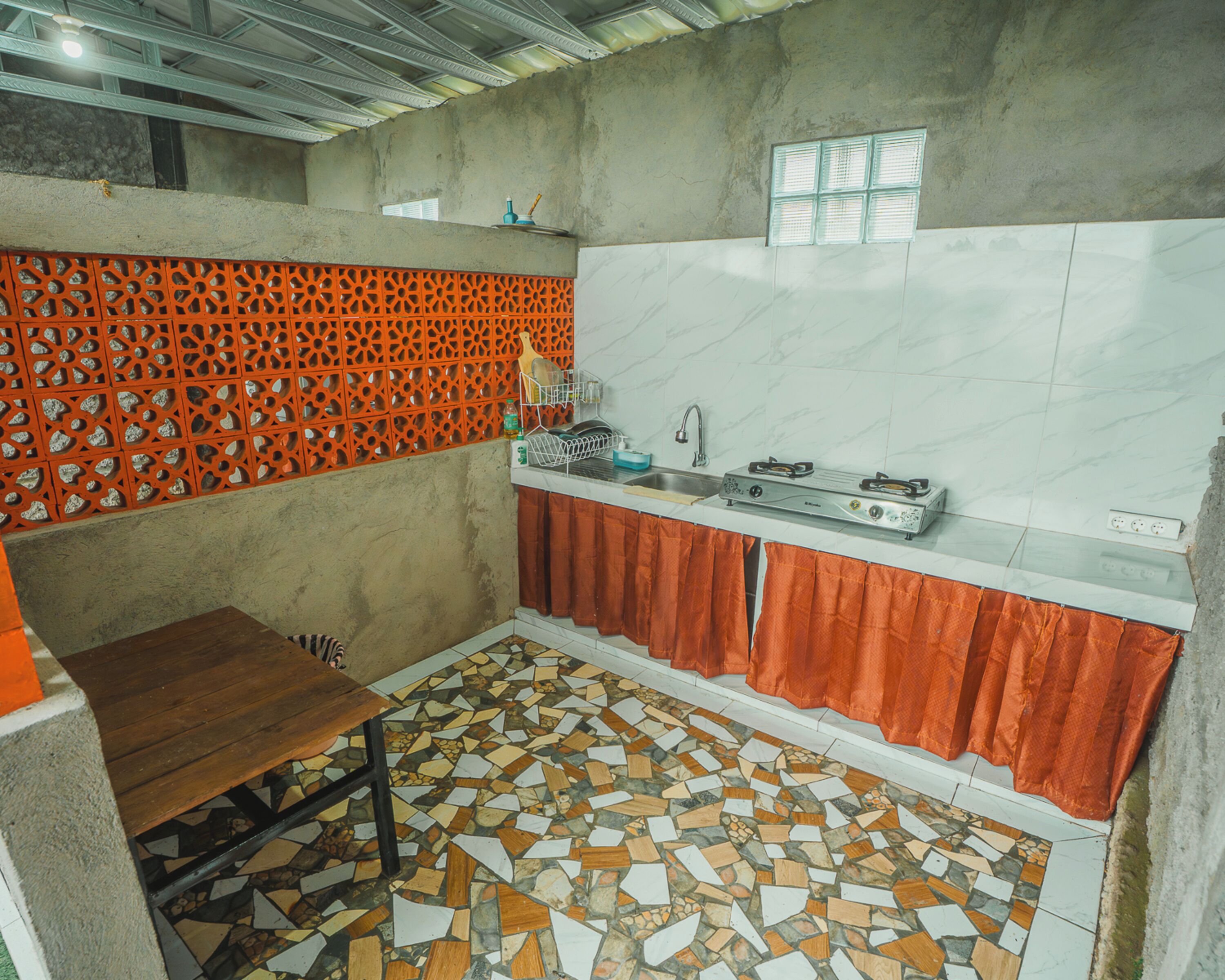 Uma cozinha compacta com painel de azulejos, pia, fogão e uma pequena mesa de jantar.