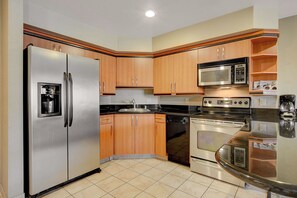 Uma cozinha com eletrodomésticos de aço inoxidável, armários de madeira e piso revestido de azulejos.