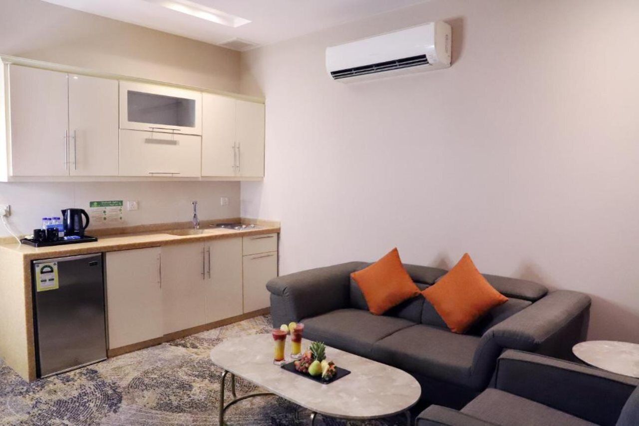 Um espaço compacto com cozinha compacta, um sofá com almofadas laranja e uma pequena mesa de centro.