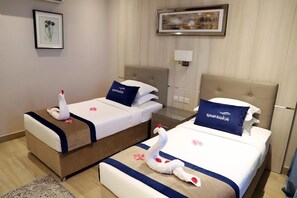 Quarto de hotel com duas camas, cada uma com toalha em formato de cisne e almofada com logótipo.