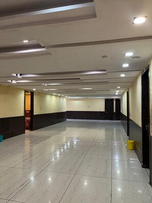 Um corredor amplo com piso ladrilhado, iluminação embutida e uma porta que dá para outro cômodo.