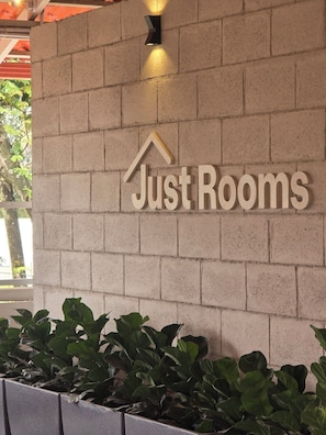 Parede com uma placa que diz 'Just Rooms' e um vaso com folhagem verde.