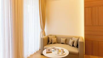 Quarto moderno com sofá, mesa redonda pequena e uma janela com cortinas leves.