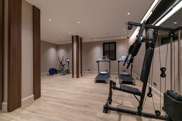 Uma academia com equipamentos de cardio, aparelhos de musculação e um espelho grande.