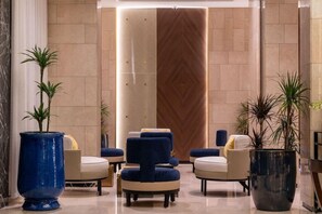 Um hall com design moderno, com área de estar com sofás e poltronas, painel de parede de madeira grande e plantas em vasos.