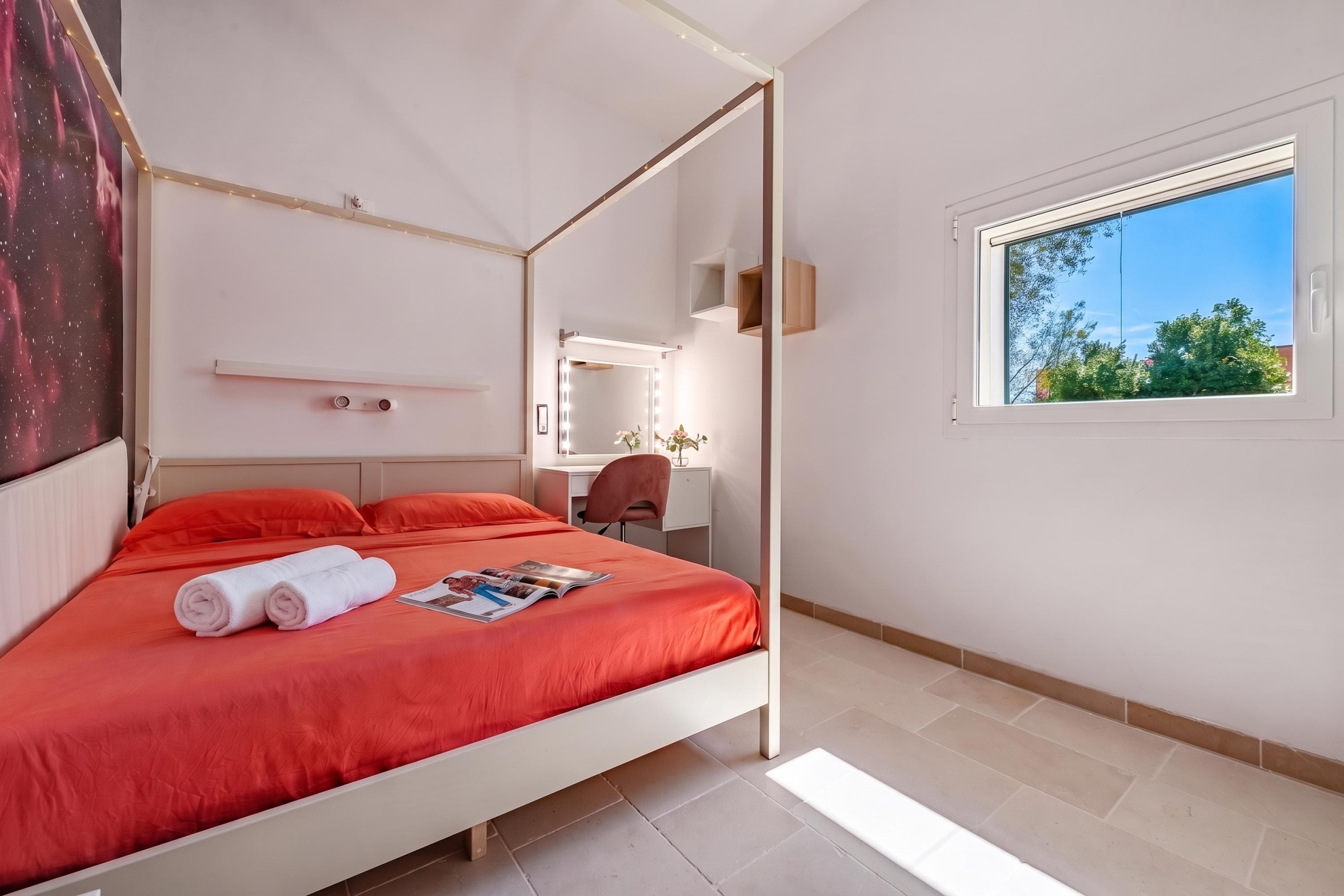 Quarto com cama, escrivaninha, cadeira, janela e espelho.