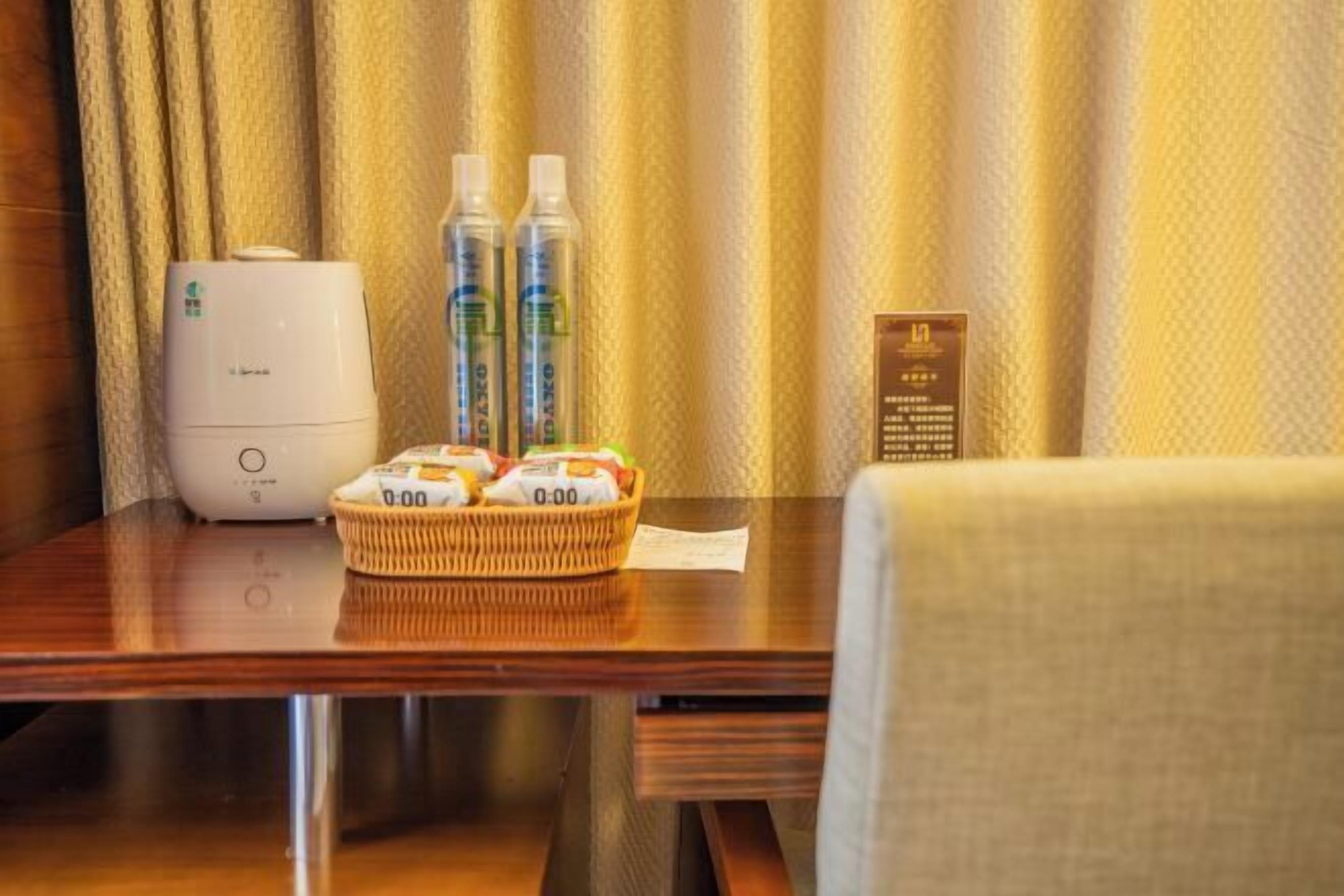 Quarto de hotel com uma escrivaninha de madeira, um cesto de produtos de higiene e um purificador de ar fixado na parede.