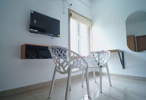 Quarto com televisão de tela plana presa à parede, janela com moldura de madeira e duas cadeiras brancas com design vazado.