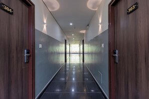 Corredor com portas indicando os números 304 e 303, que dá passagem para uma área luminosa com luz natural.