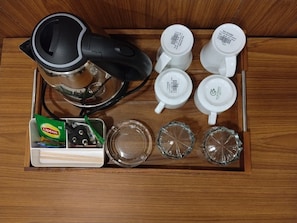 Uma gaveta com uma cafeteira, seis canecas brancas, um sachê de chá Lipton e duas tampas de vidro.